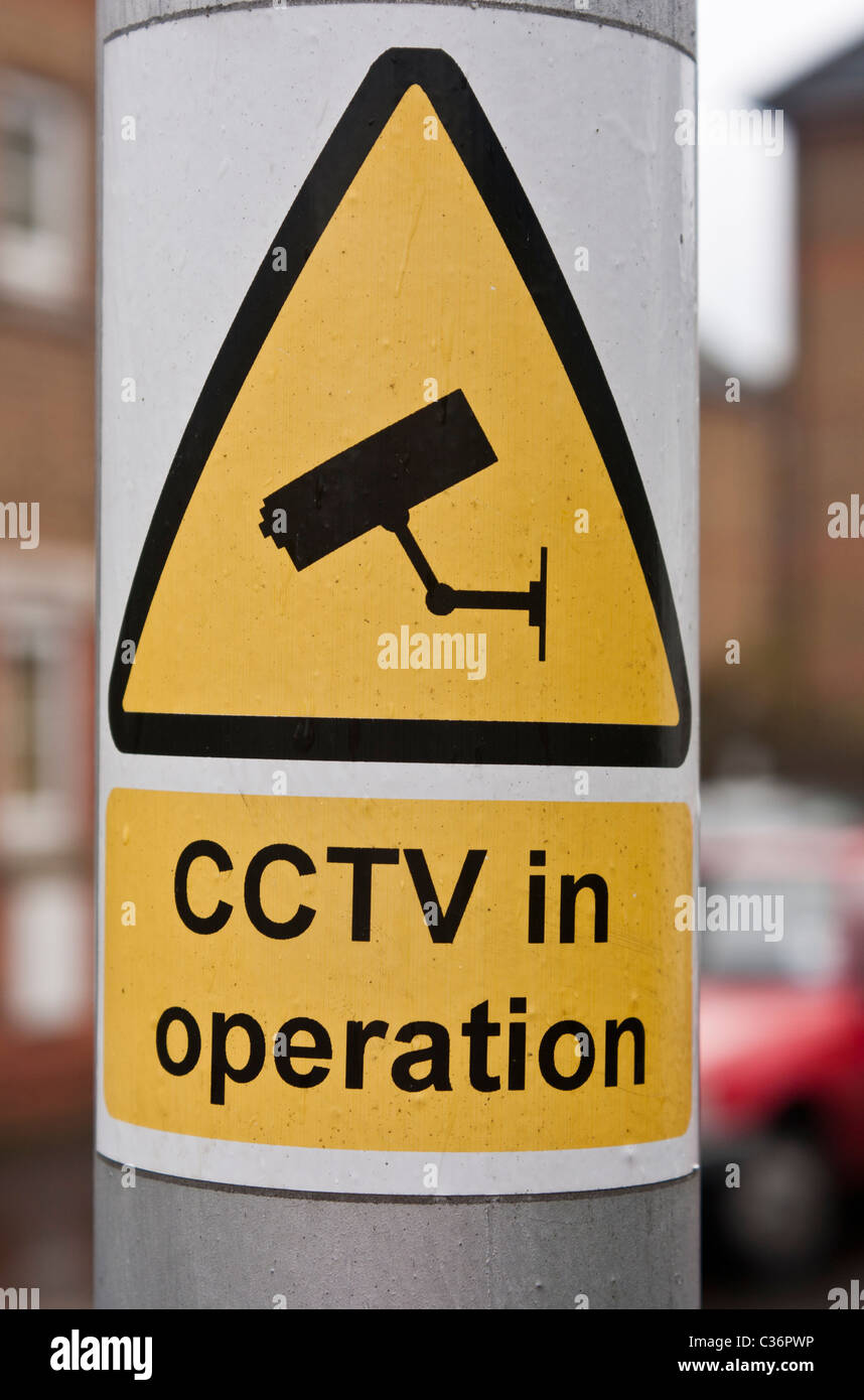 A yellow triangular 'CCTV in Operation' sticker on a lamppost in an ...