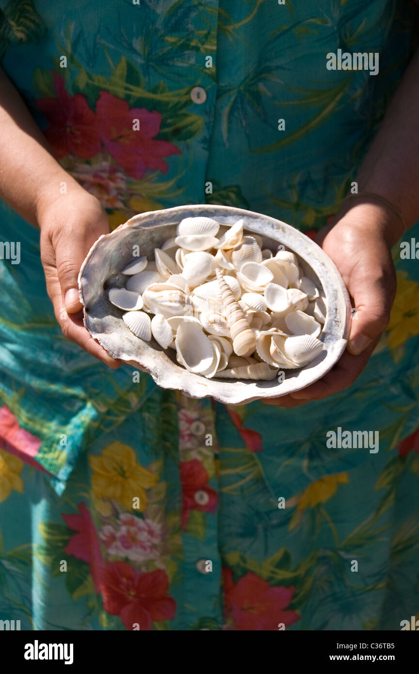 A woman holding a an abalone shell filled with a mixture of other ...