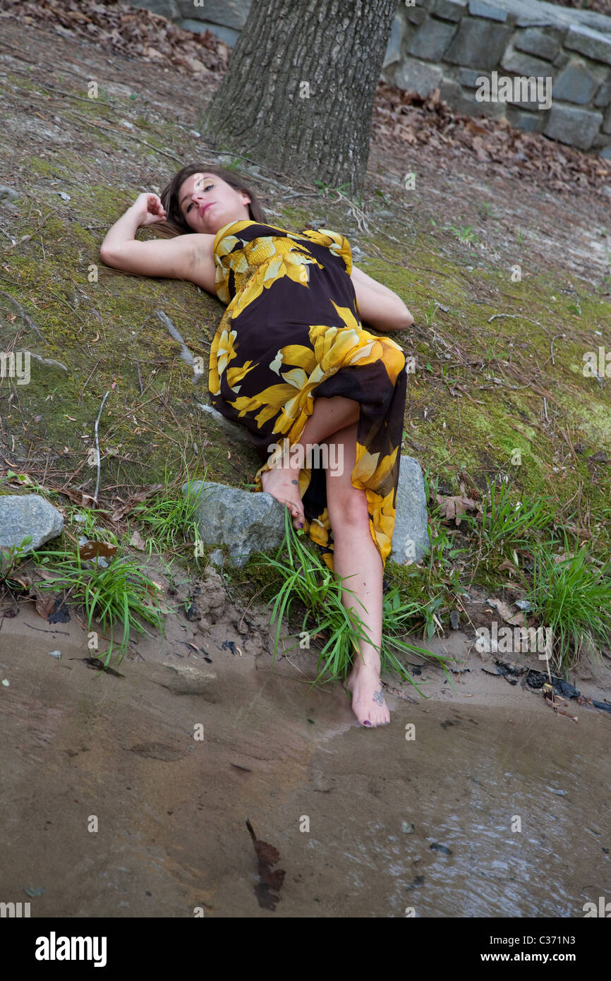 Pretty woman laying on a mossy bank beside a quiet stream with eye ...