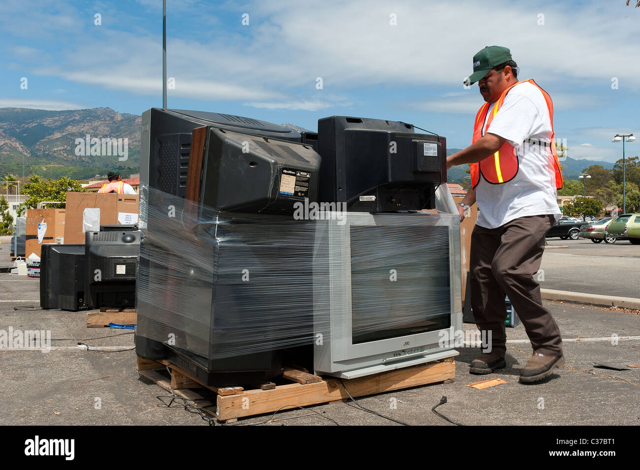 Recycling worker is wrapping with plastic a palette of old televisions ...
