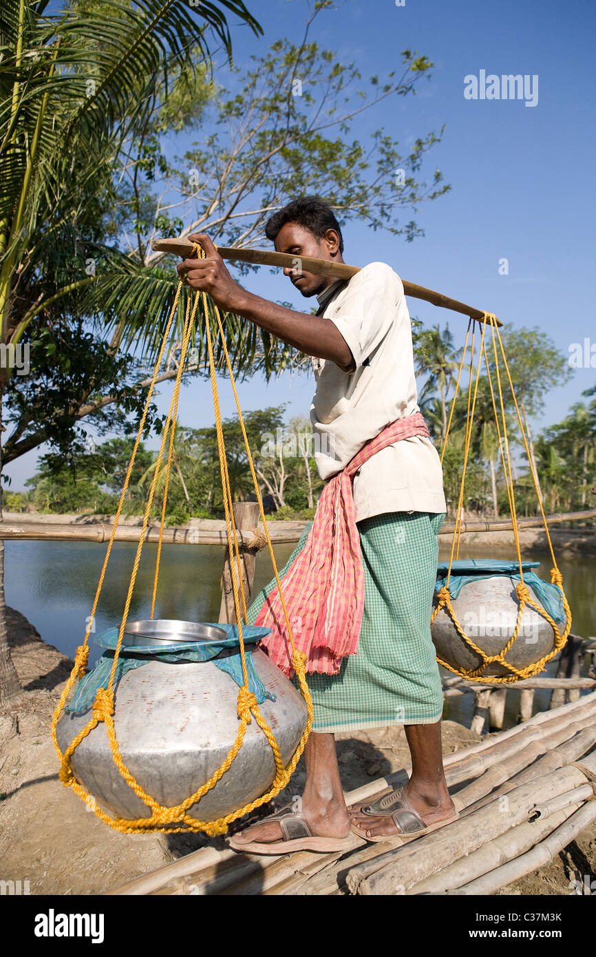 Indian man is carrying pots of water in a small village in the ...
