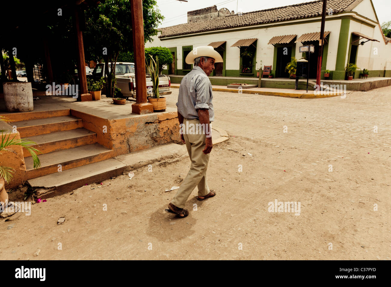 A Mexican man in a white hat walks on a dusty street in the village of ...