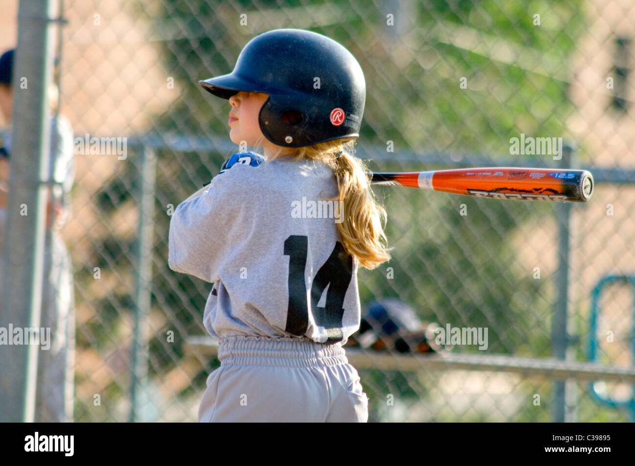 Young girl up for batting in baseball game wearing safety helmet. St ...