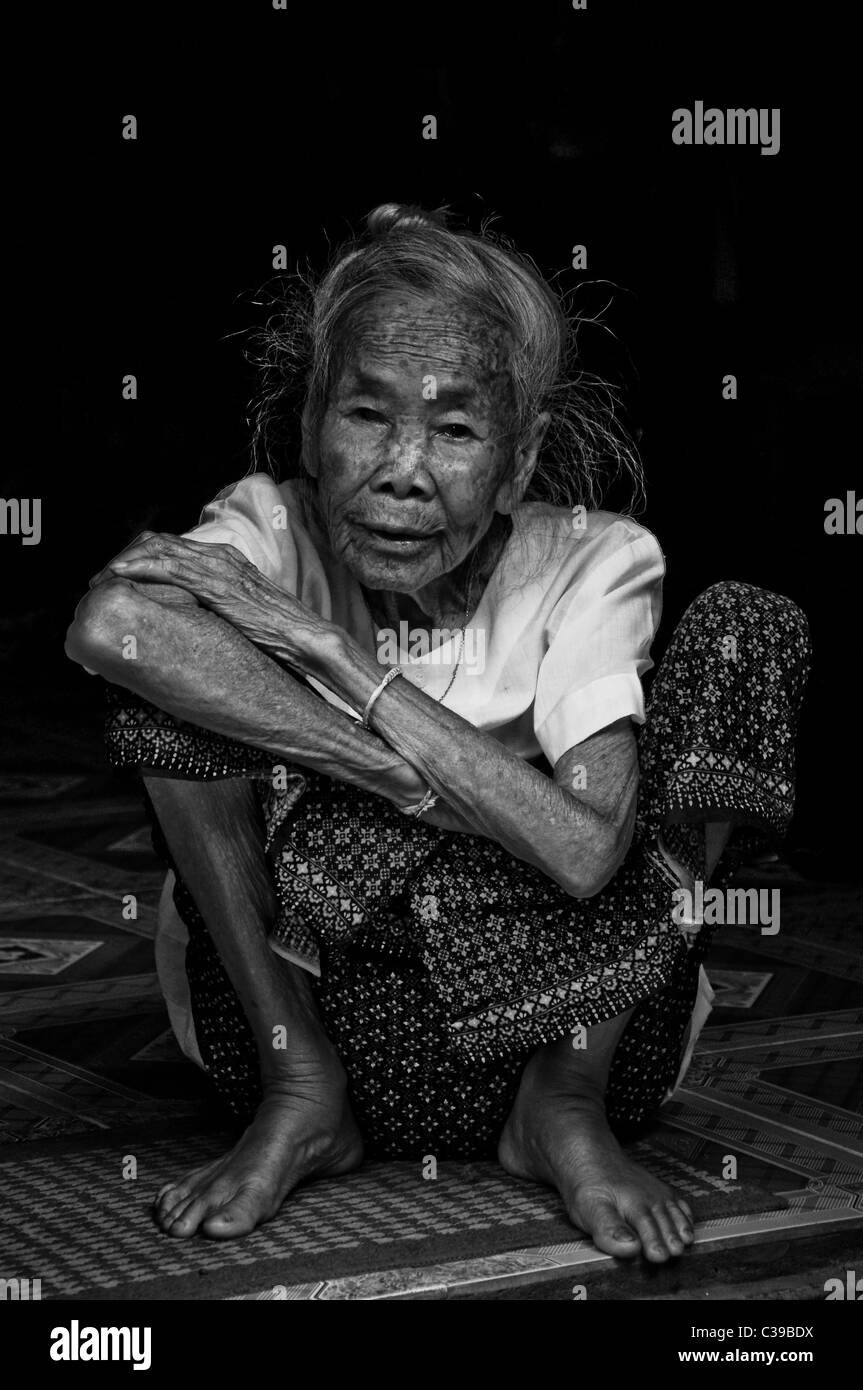 Elderly woman sits on her haunches in her home on the Mekong River ...