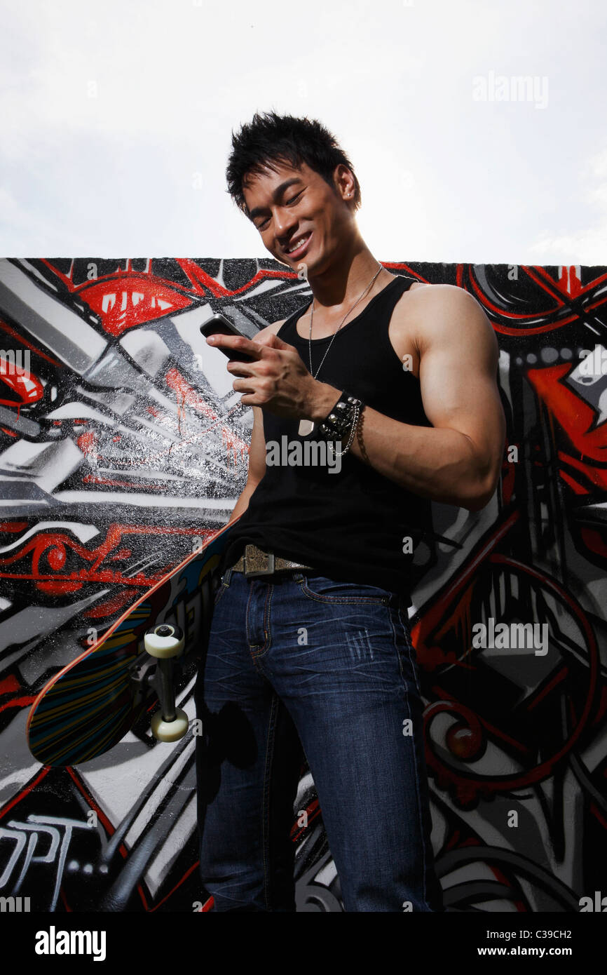 Young man standing in front of graffiti wall texting on phone while ...