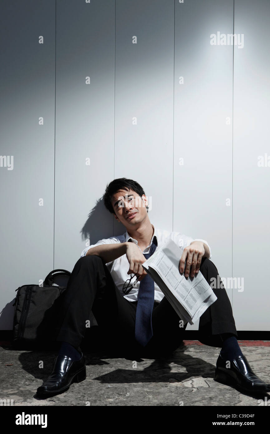 Chinese man sitting on ground holding newspaper and looking sad Stock ...
