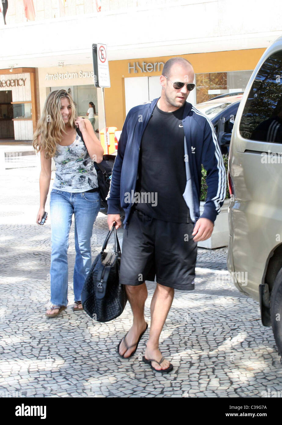 Jason Statham, wearing sunglasses, shorts and flip flops, escorted by ...