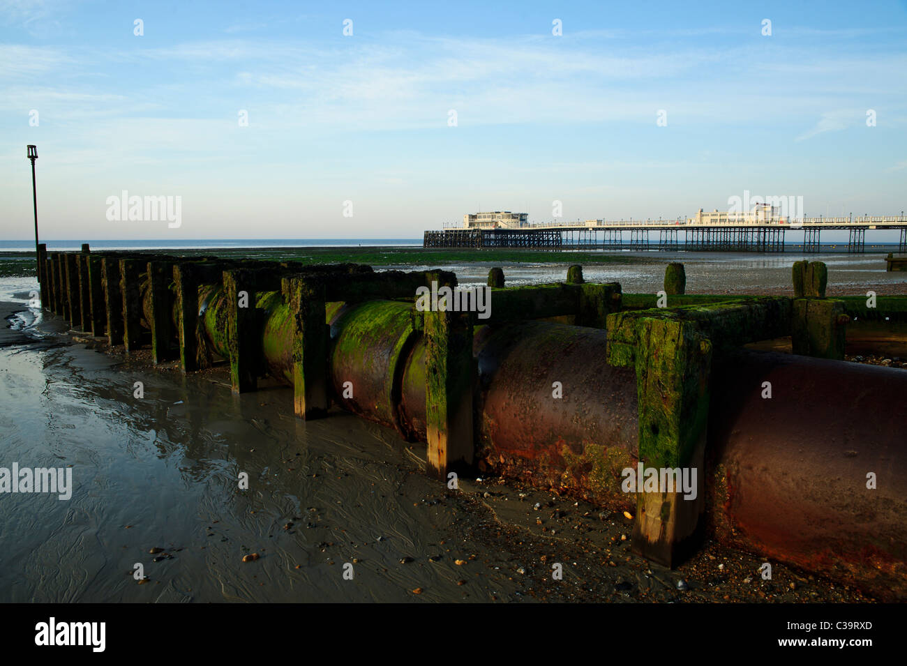 A rusting storm water outfall on Worthing beach with the Art Deco Pier ...
