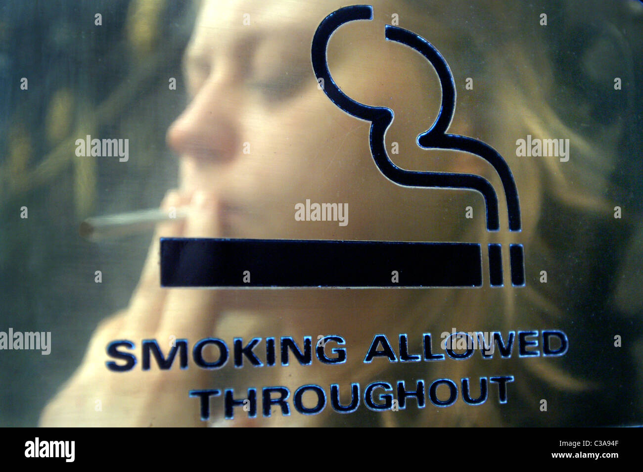 A young woman having a cigarette break at a "Smoking allowed" sign ...