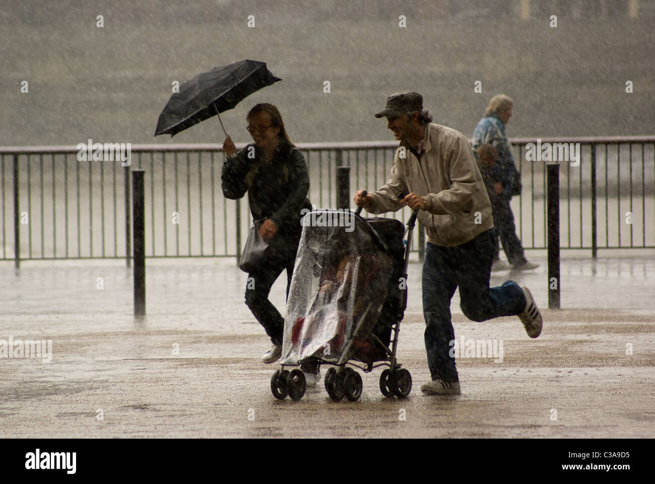 Couple running through torrential rain, and pushing toddler in pram ...