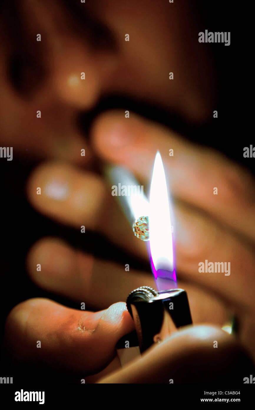 A close-up picture of a man lighting a cigarette, his face solely lit ...