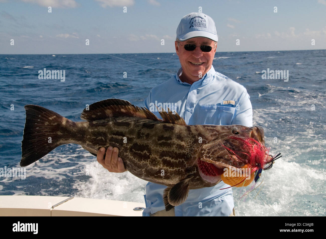 An angler lifts his nice catch, a big grouper, caught off the beach in ...