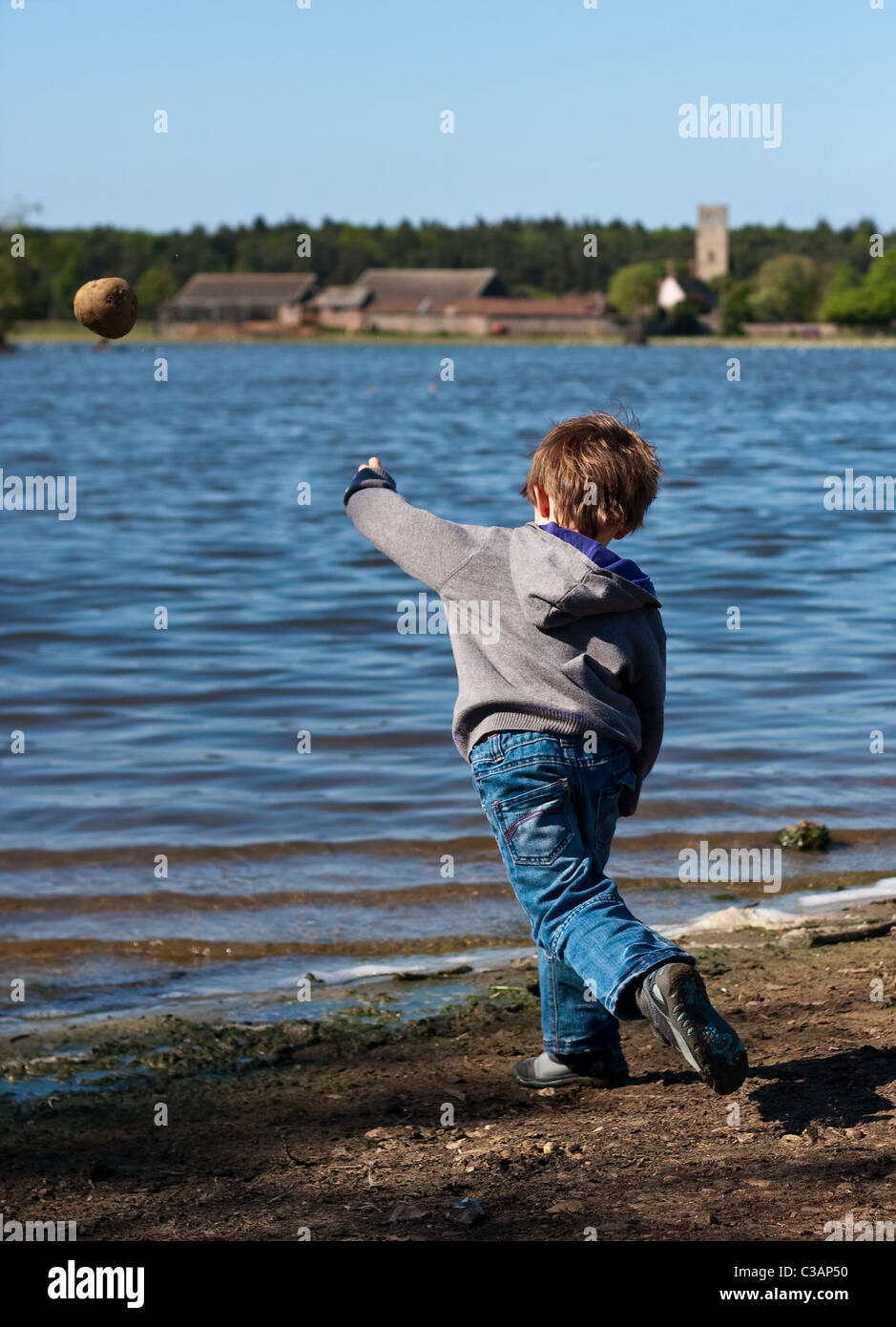 Little boy throwing objects into a lake at Ampton, Suffolk Stock Photo ...