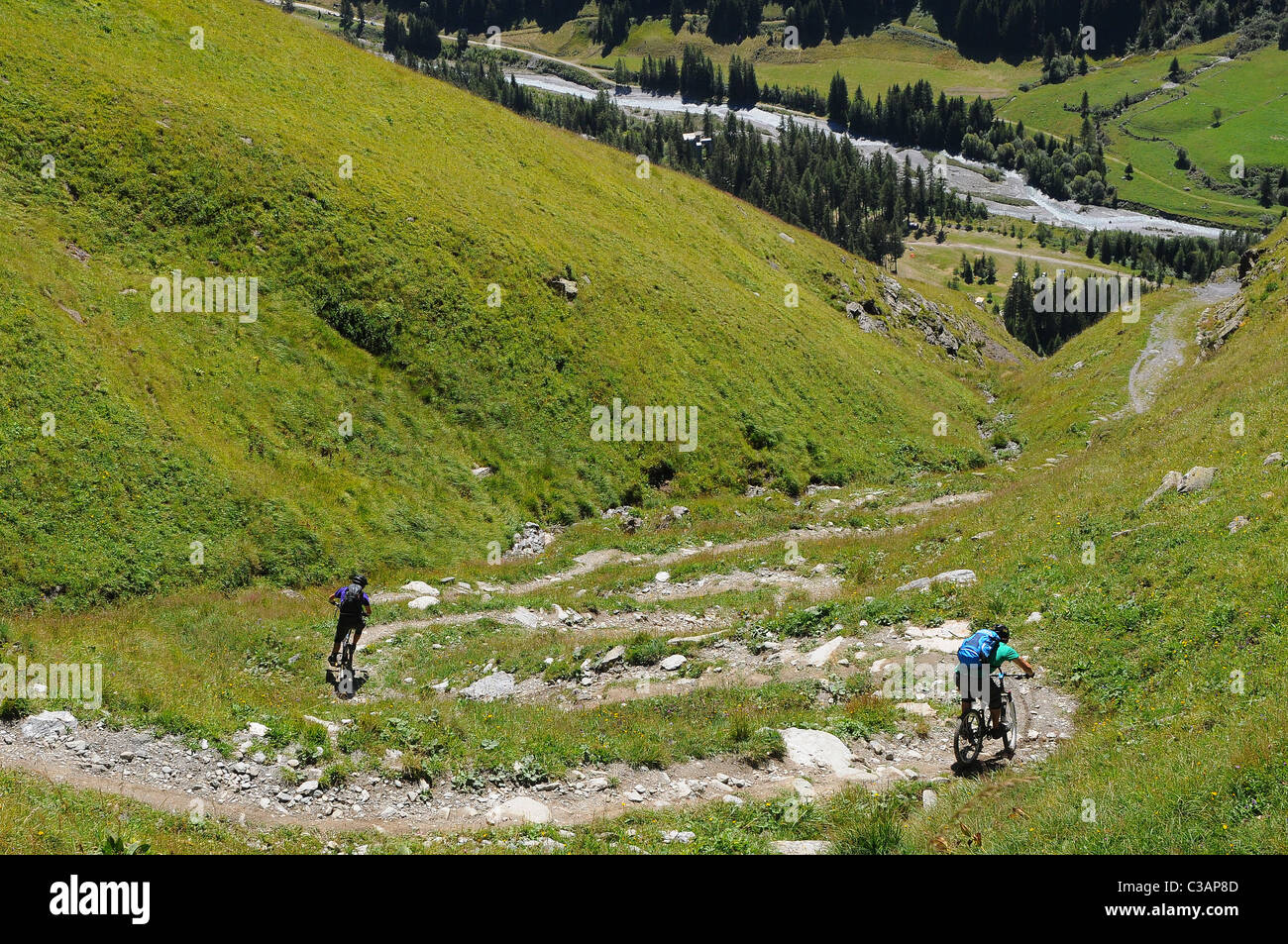 Two mountain bikers ride down a winding path high above the village of ...