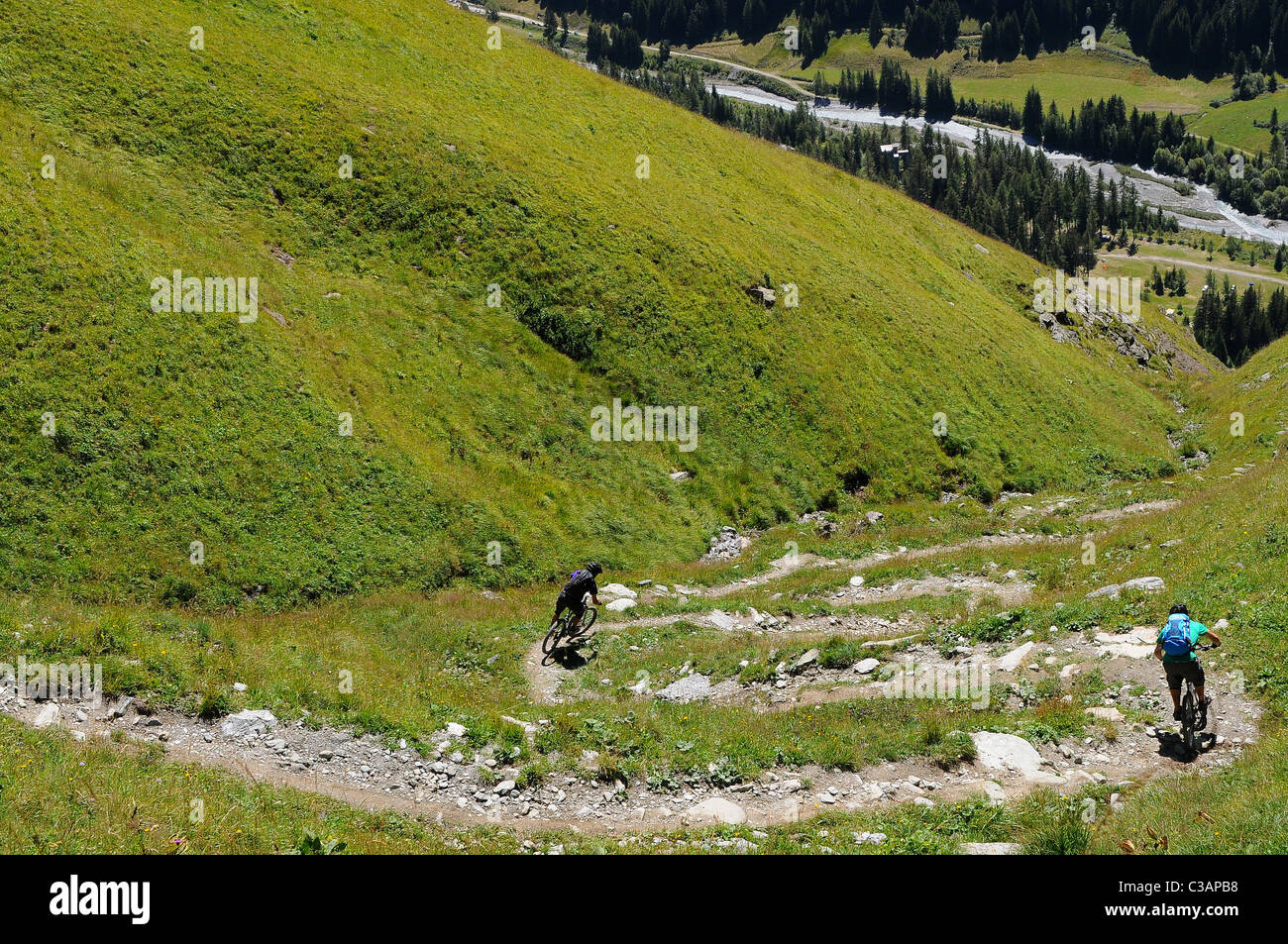 Two mountain bikers ride down a winding path high above the village of ...