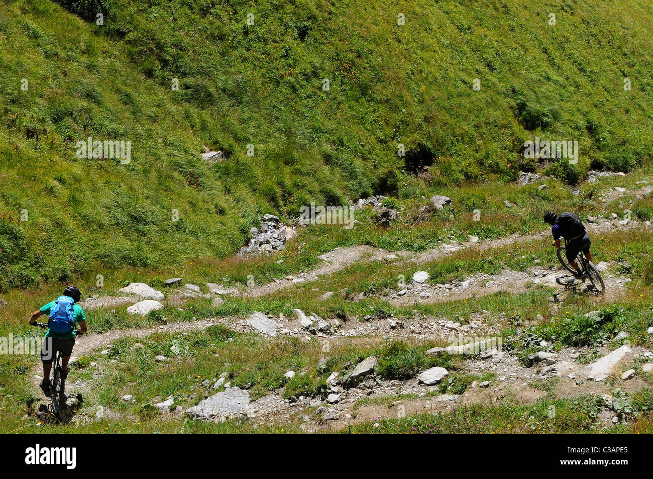 Two mountain bikers ride down a winding path high above the village of ...