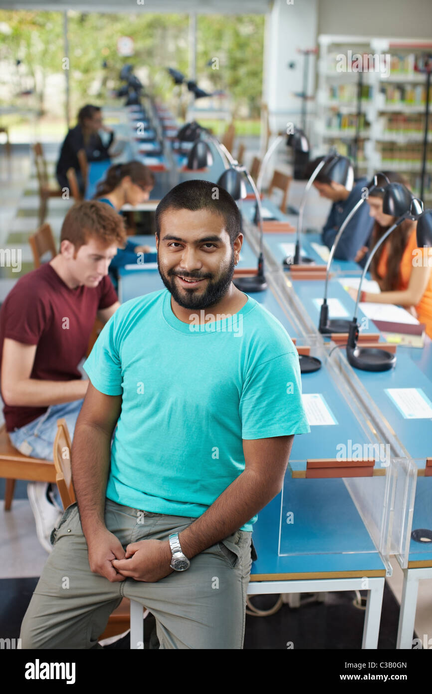 portrait of male college student sitting on table in library and ...