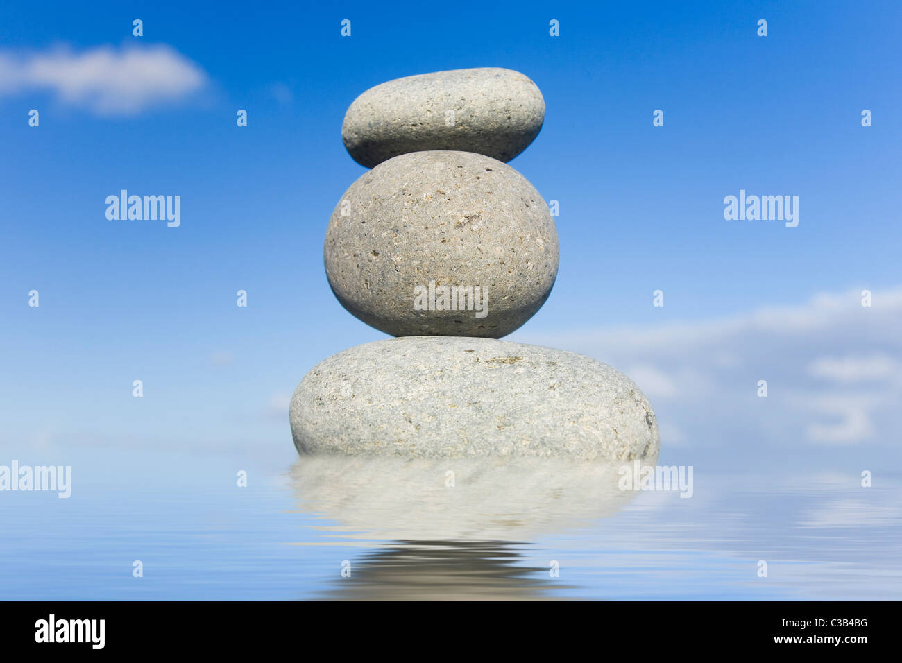 Stack of zen pebbles reflected in still water with a blue sky behind ...