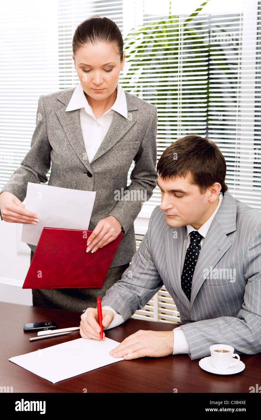 Portrait of serious boss signing contract with executive secretary near ...