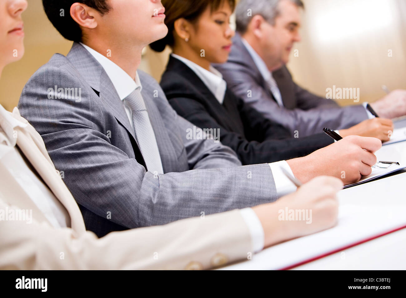 Row of business people making notes during conference Stock Photo - Alamy