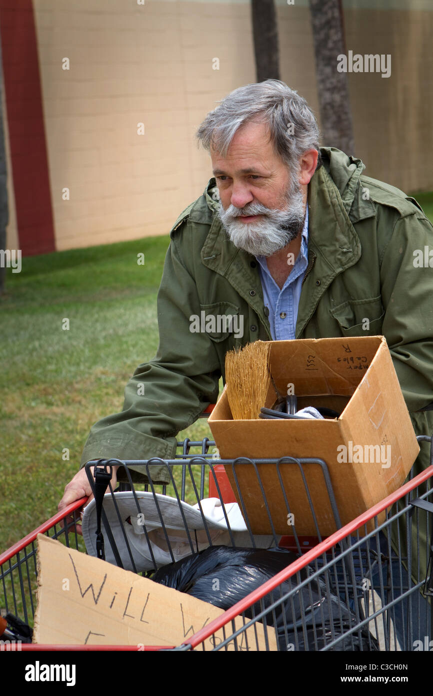 Homeless man wearing an old army coat pushes a shopping cart holding ...