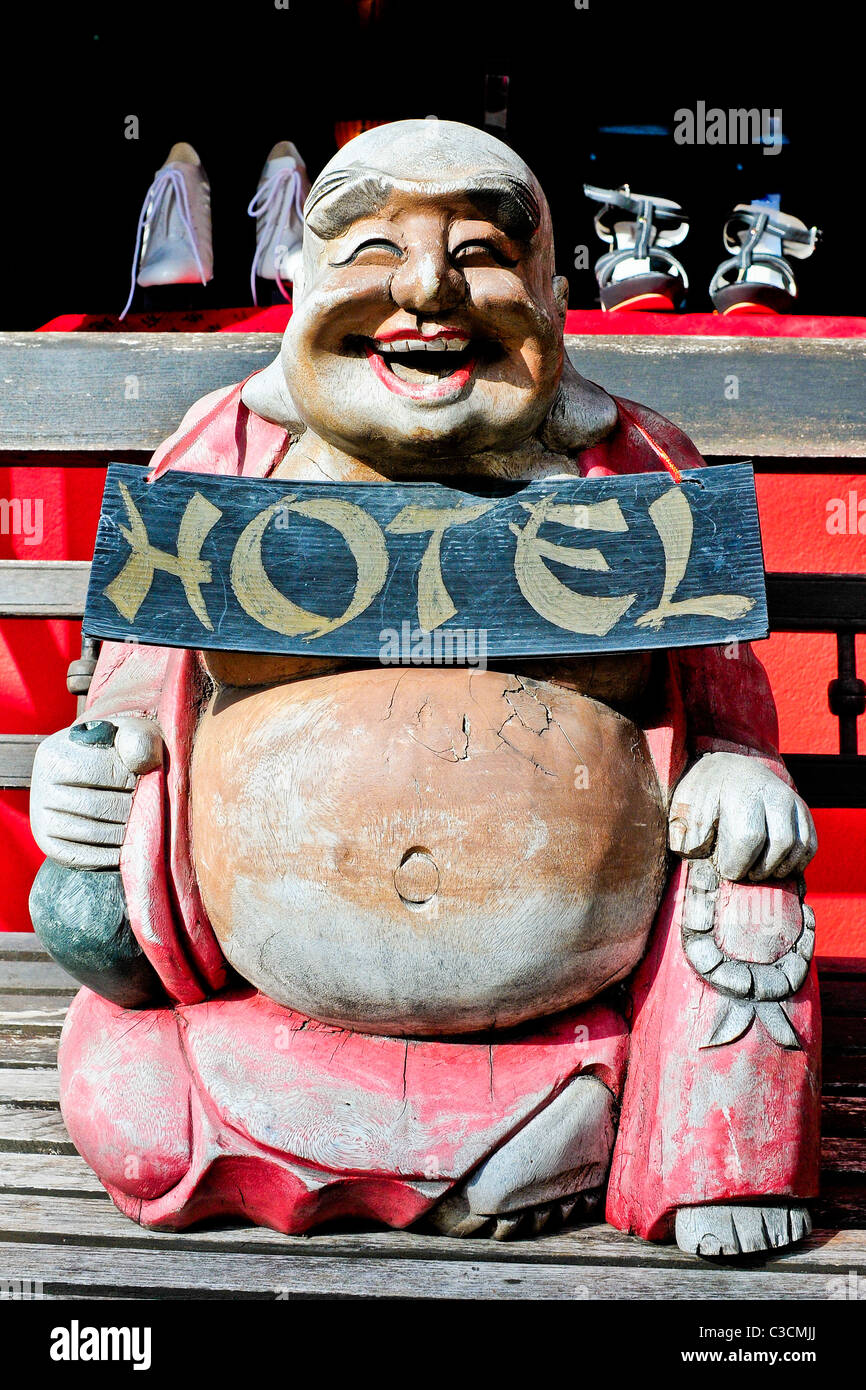 A carved fat man in an Asian style holds a "HOTEL" sign Stock Photo - Alamy