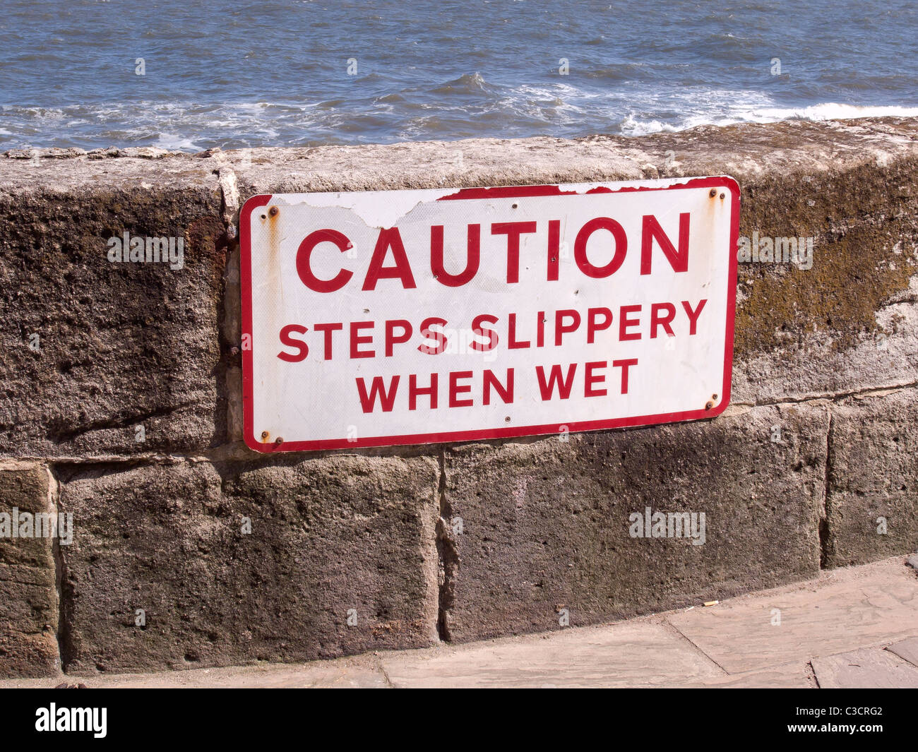 Warning sign Caution Steps Slippery when Wet on a stone harbour wall ...