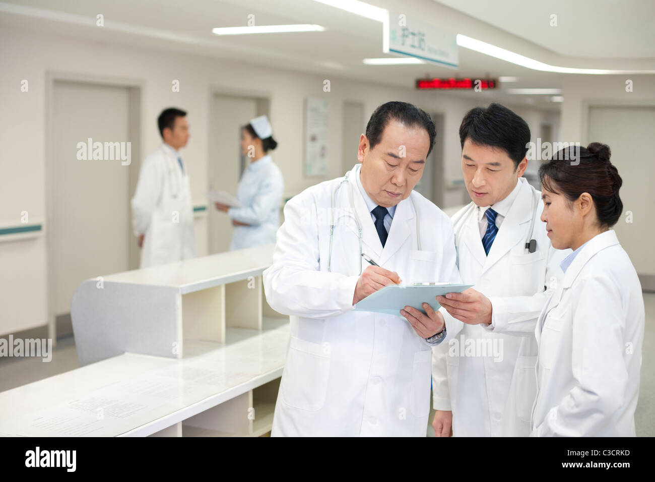 An older doctor fills out a form with fellow doctors Stock Photo - Alamy