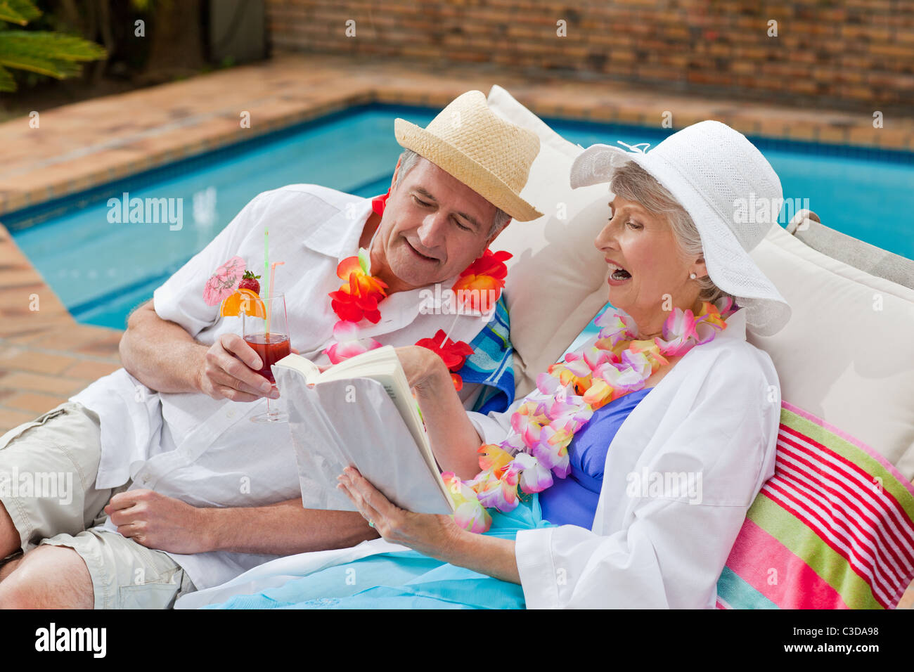 Mature woman reading a book while her husband is drinking a cocktail ...