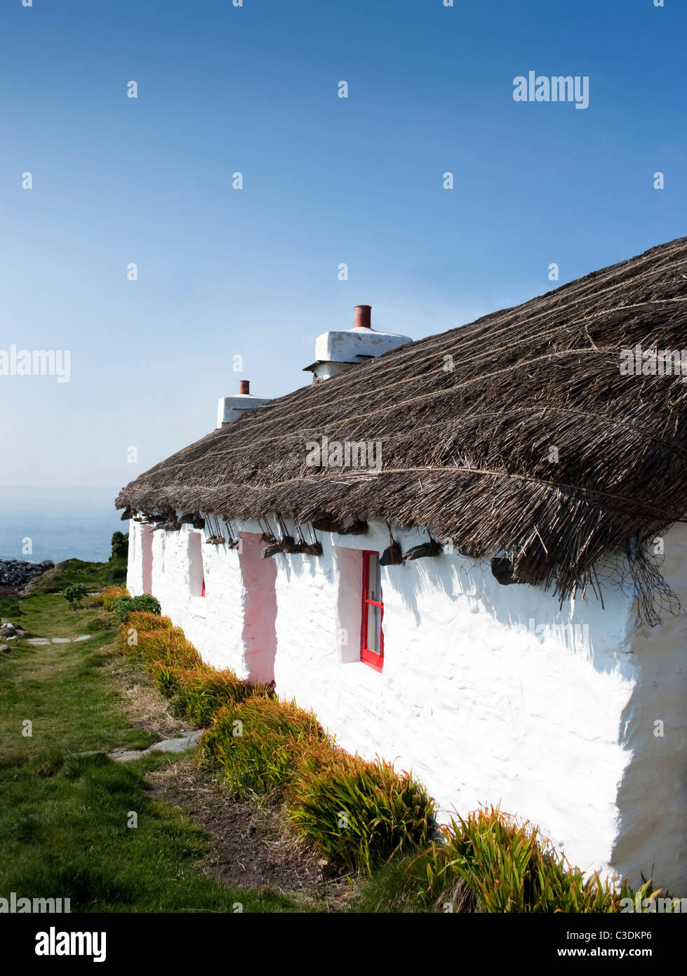Old traditional white cottage with thatched roof and red windows ...