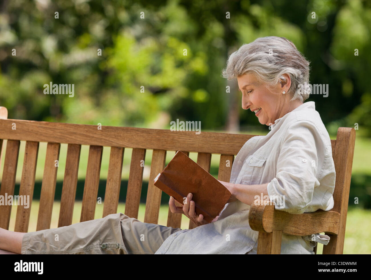 Retired woman reading a book on the bench Stock Photo - Alamy