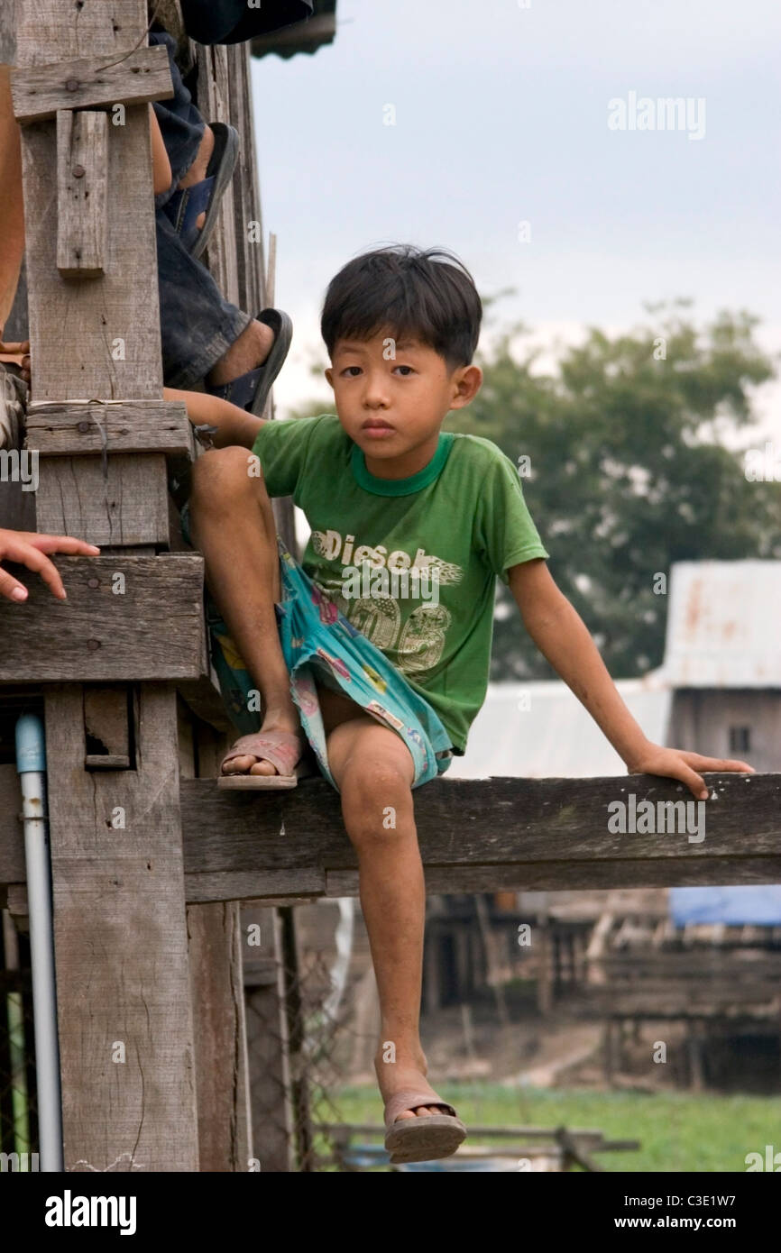 A young boy living in poverty is sitting on his rundown wooden home on ...