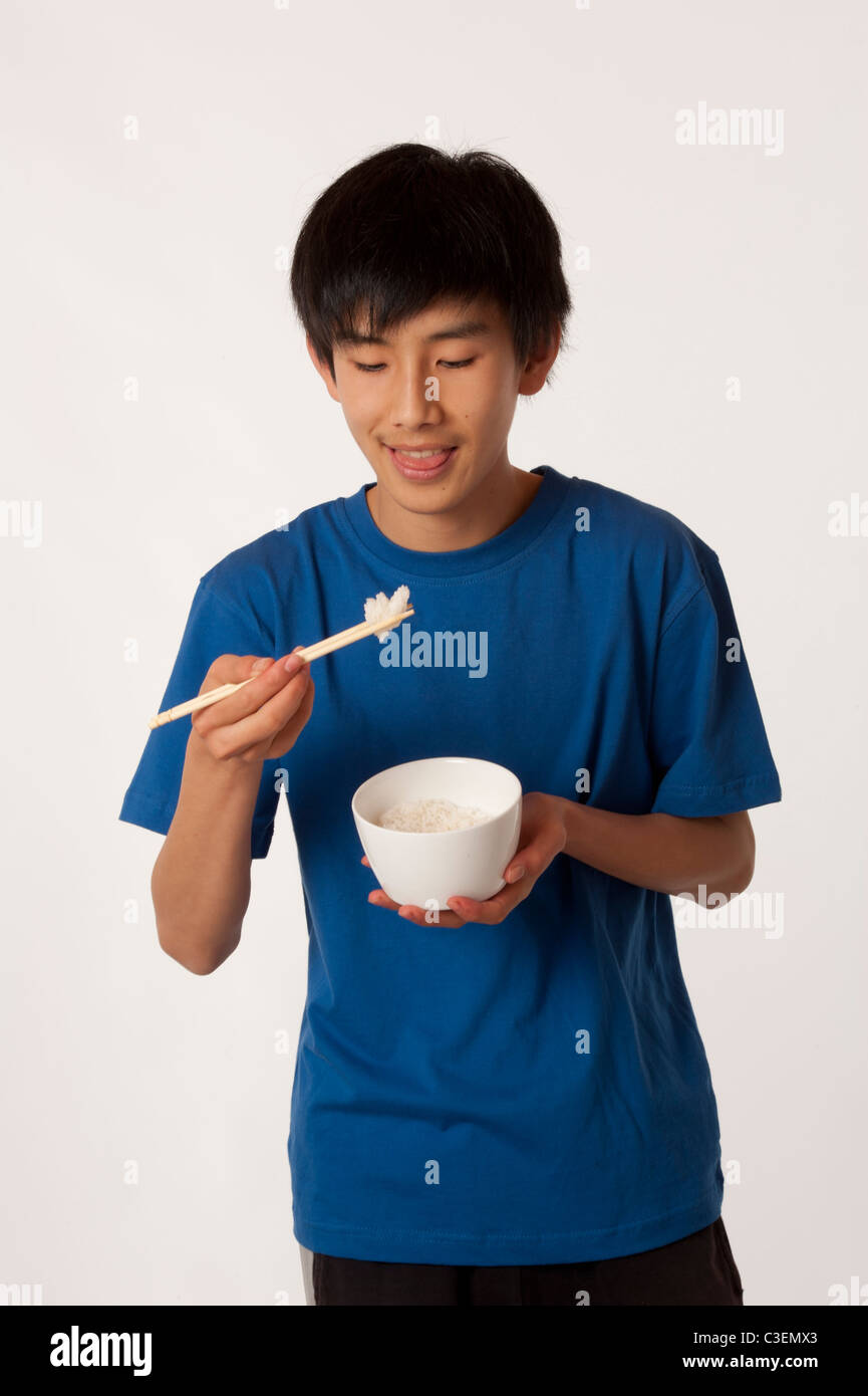 teenage Asian Chinese boy eating rice with chopsticks against white ...