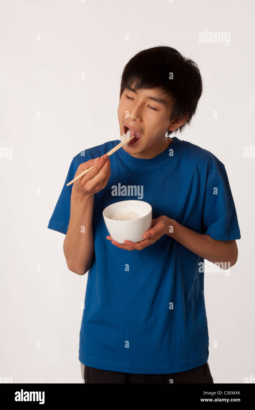 teenage Asian Chinese boy eating rice with chopsticks against white ...