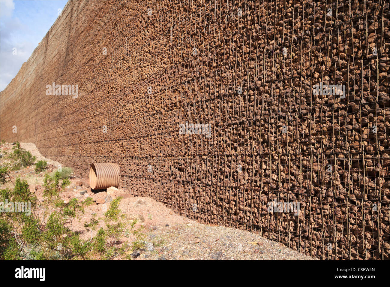 wire mesh and loose rock retaining wall with drain pipe perspective ...