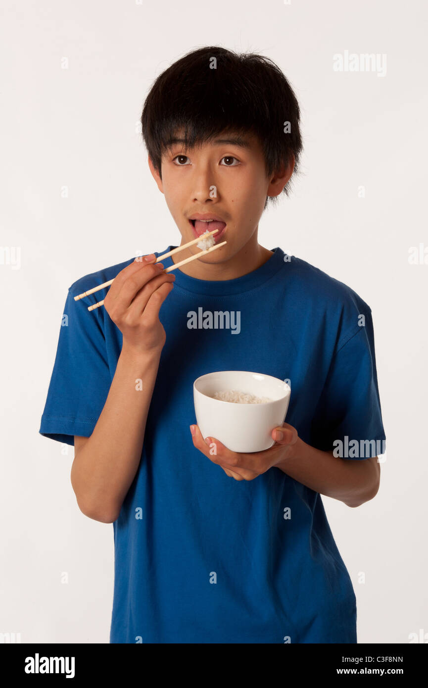 teenage Asian Chinese boy eating rice with chopsticks against white ...