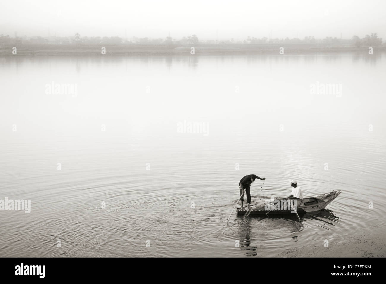 Sepia shot of a small fishing boat with two men, one rowing and one ...