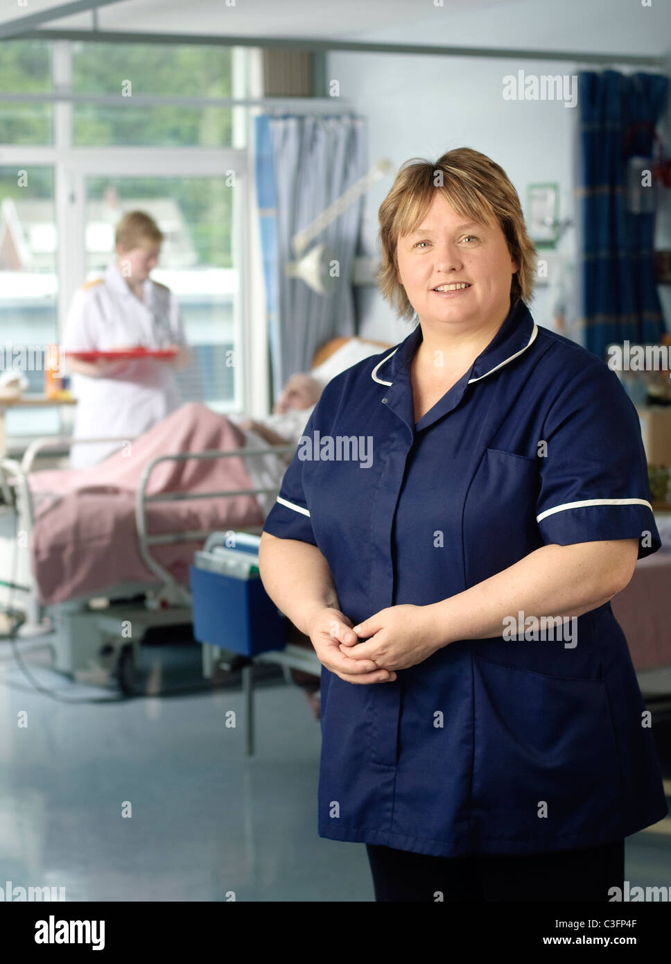 A British female Ward sister, nurse stood over-looking her ward Stock ...