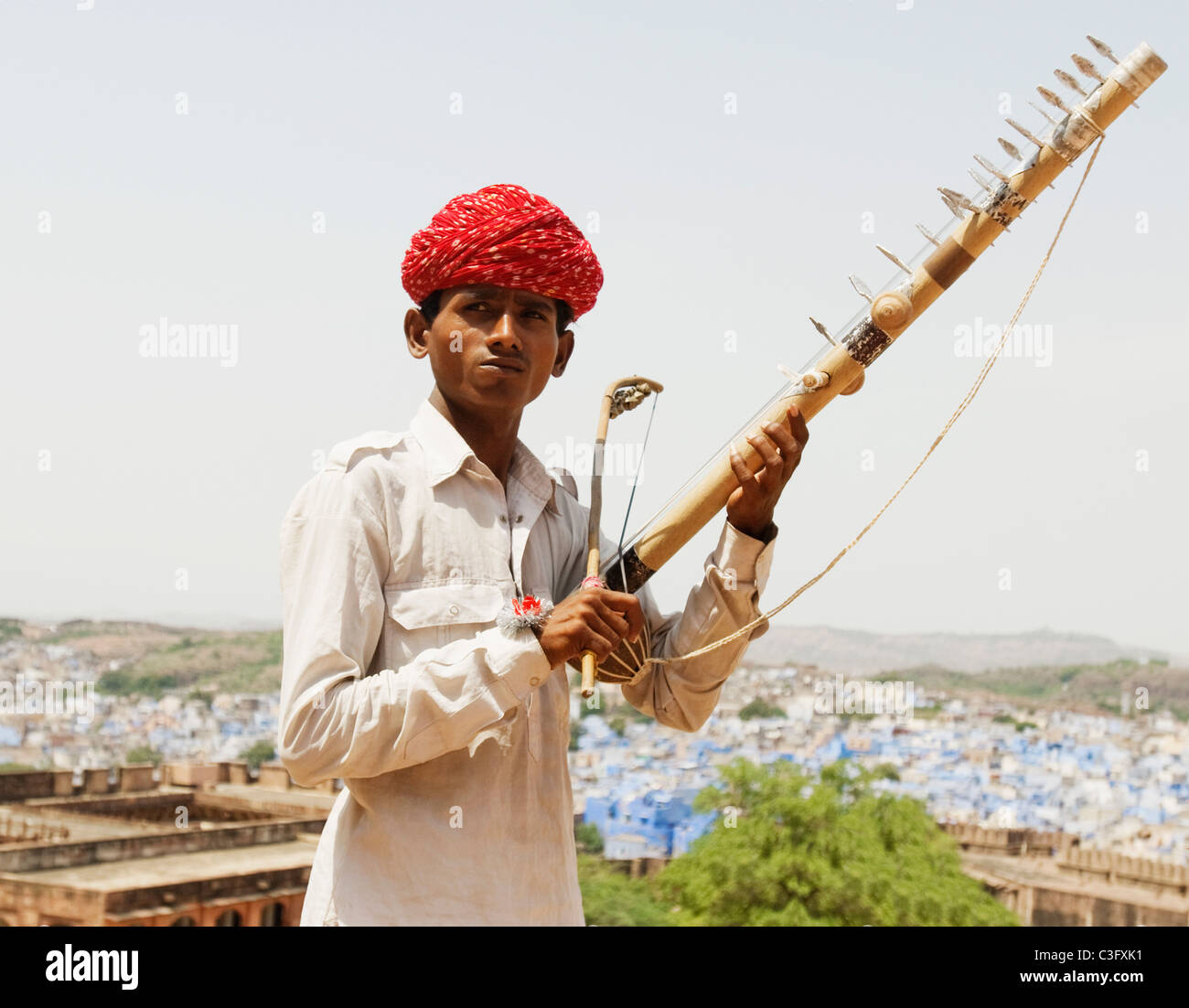 Man in traditional Rajasthani dress playing sarangi with cityscape in ...