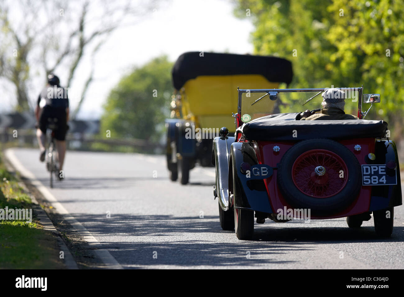 vintage cars out on a sunday drive overtake a cyclist on a country road ...