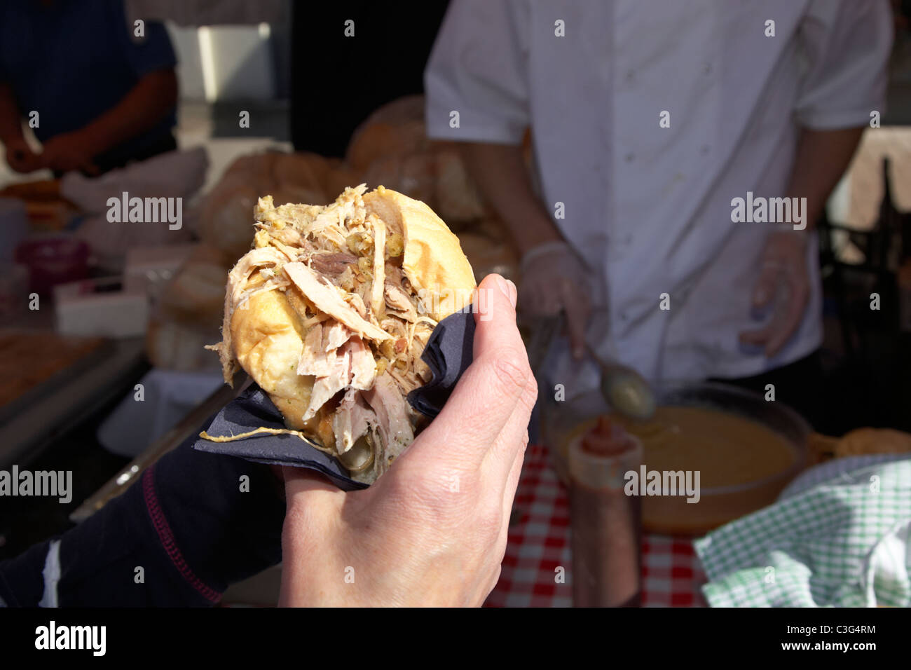 mans hand holding a hog roast pork burger bap stuffed from an outdoor ...
