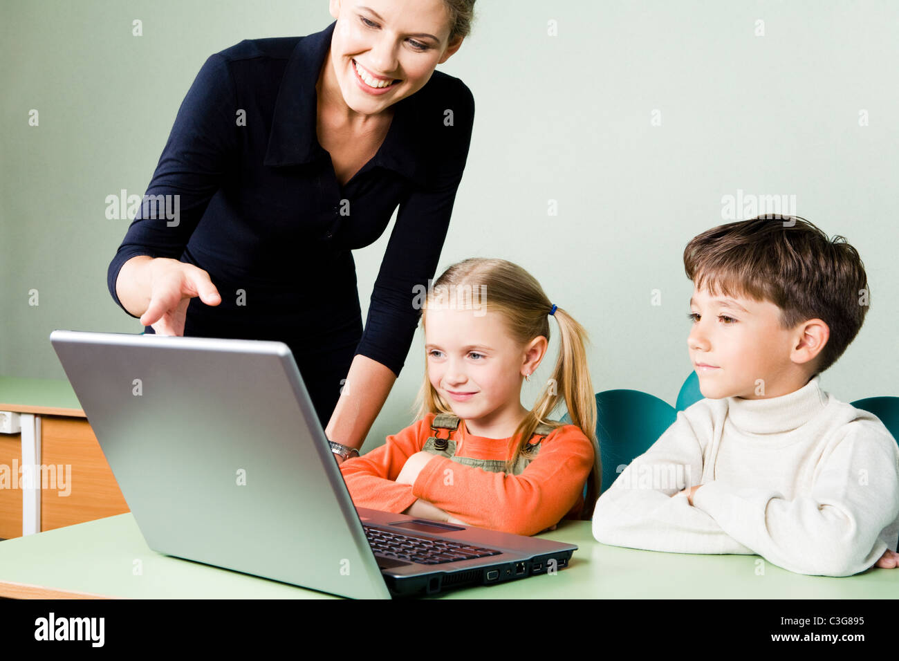 Image of two pupils looking at laptop monitor while teacher pointing at ...