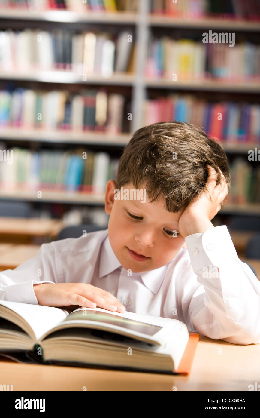 Vertical image of interested schoolkid reading book in the library ...