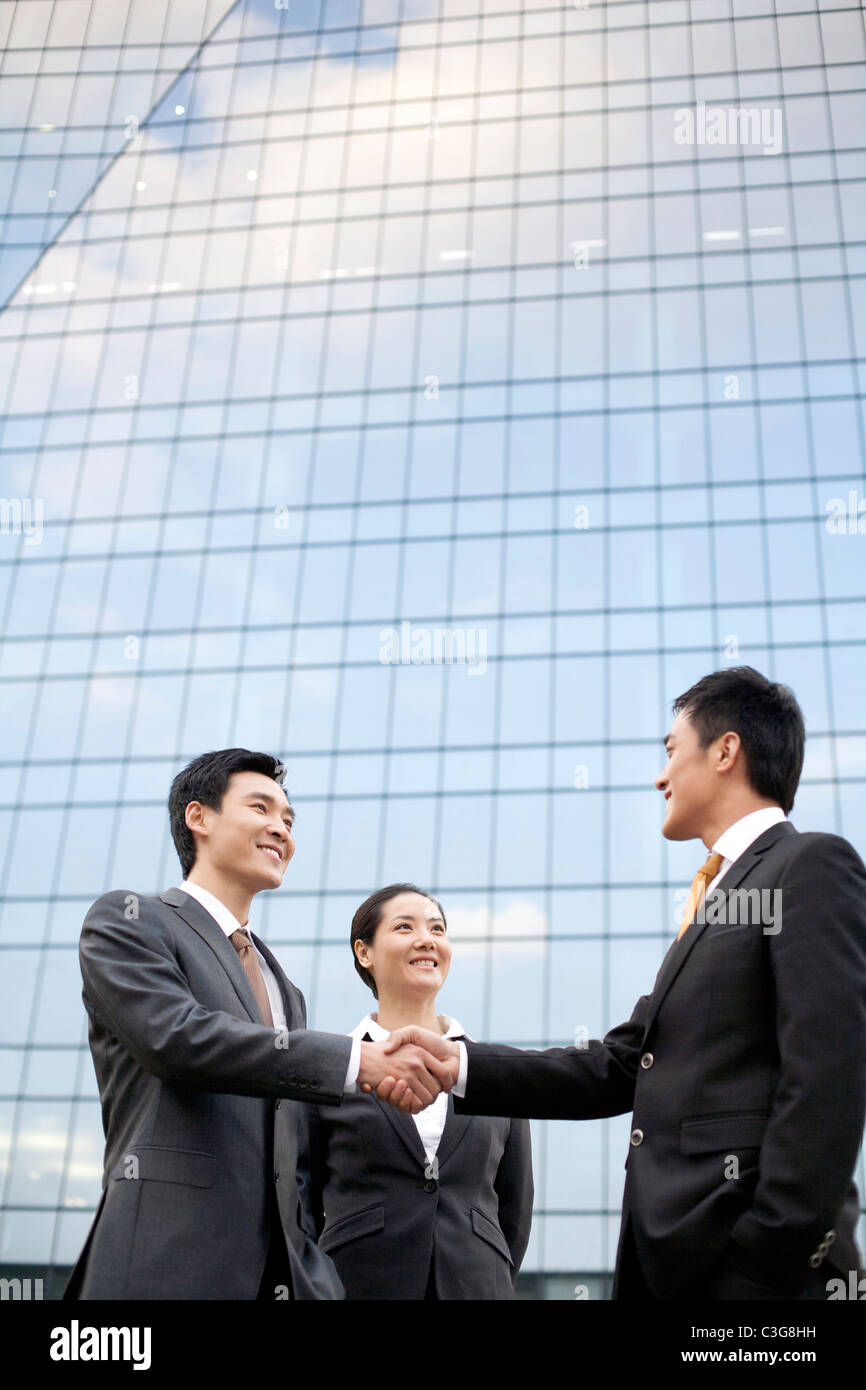 Businessmen shaking hands in front of a tall building Stock Photo - Alamy