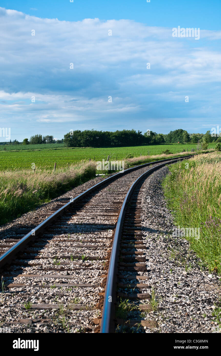 Railroad tracks curve through a green field and disappear into the ...