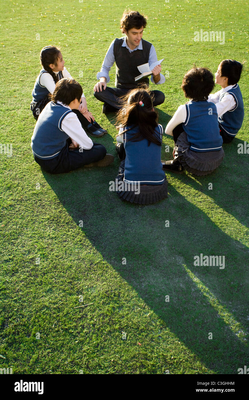 Teacher reading to students on grassy field Stock Photo - Alamy