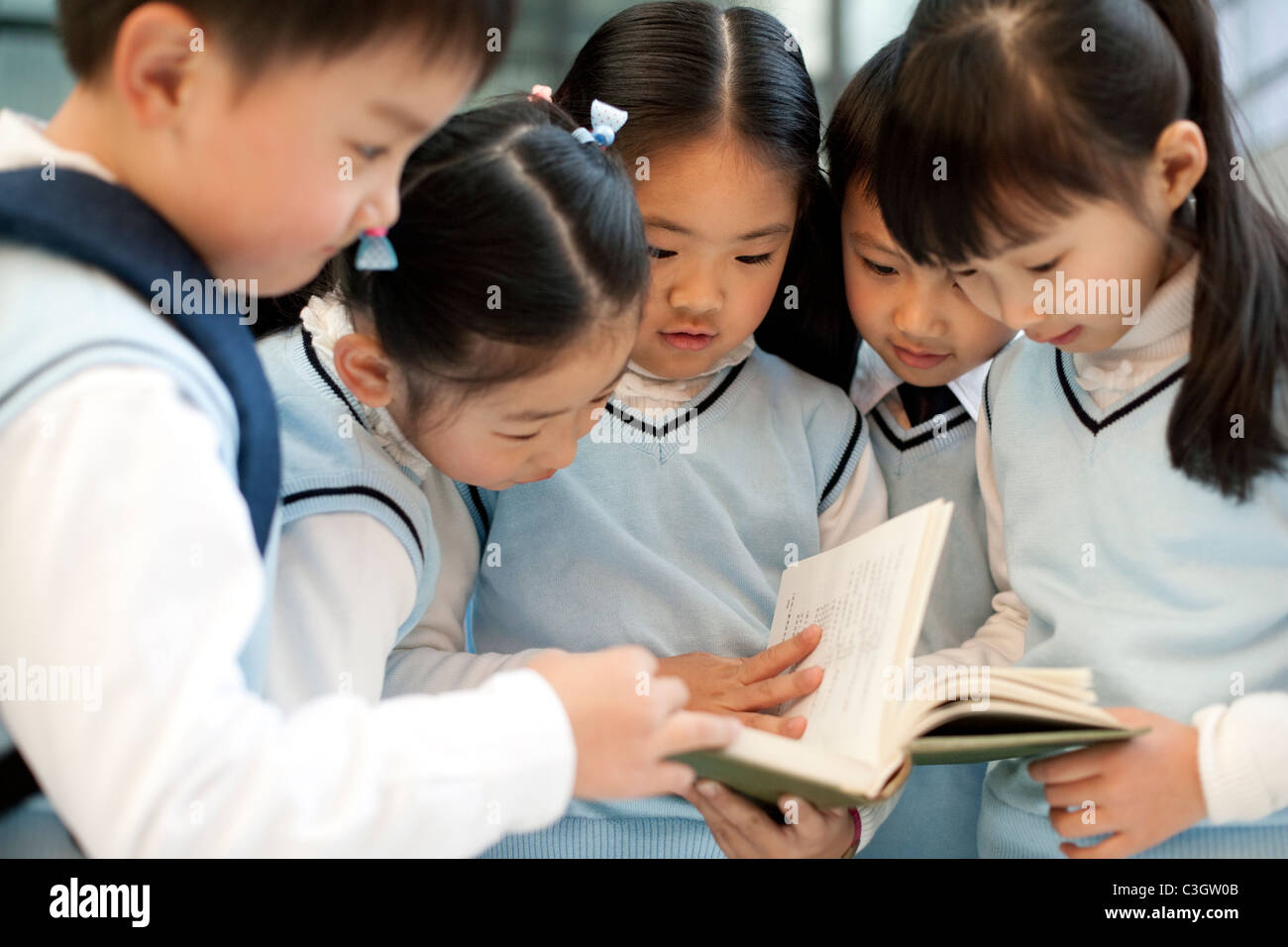 Young students huddle together reading a book Stock Photo - Alamy