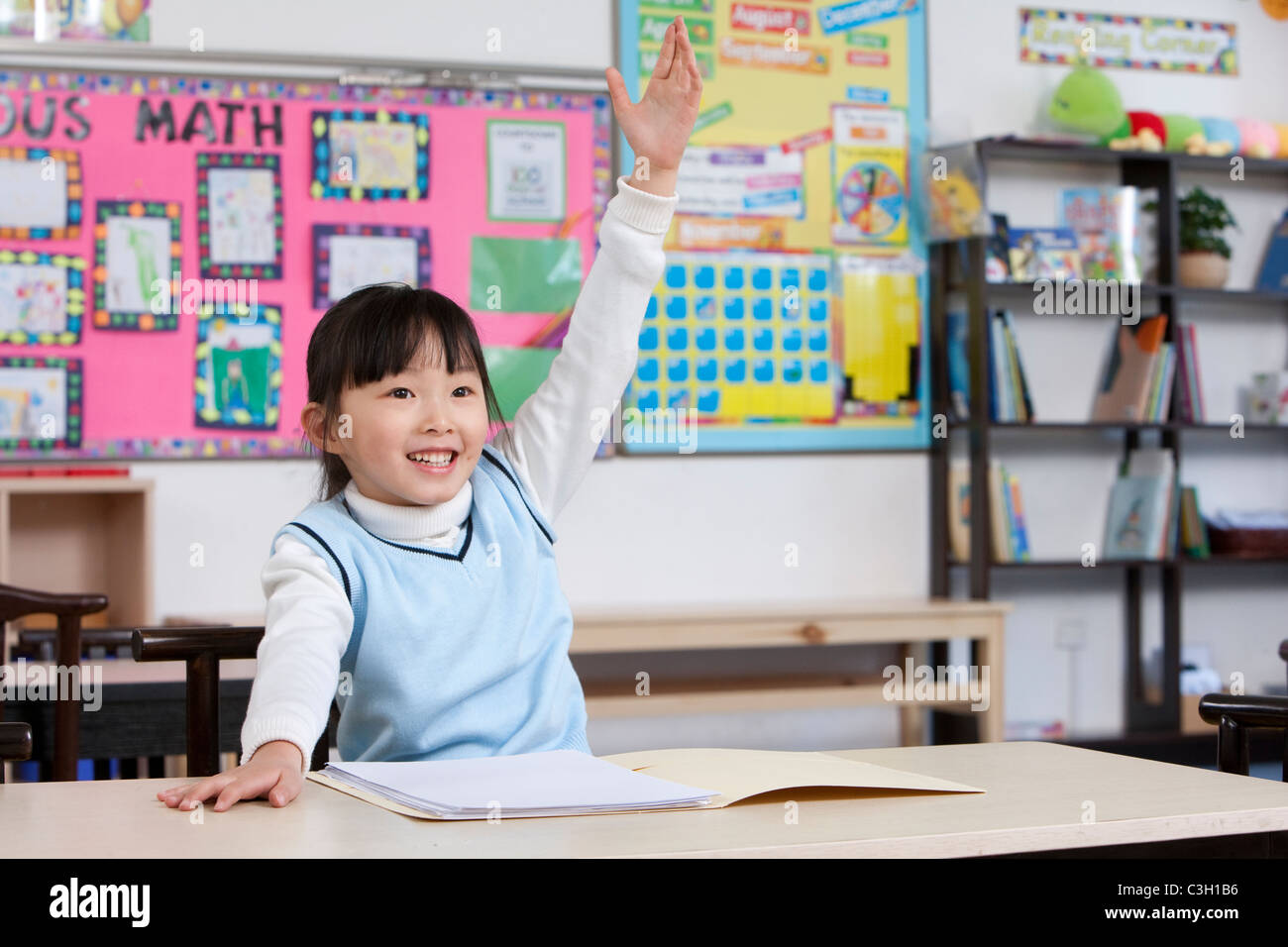 Young student raising her hand in classroom Stock Photo - Alamy