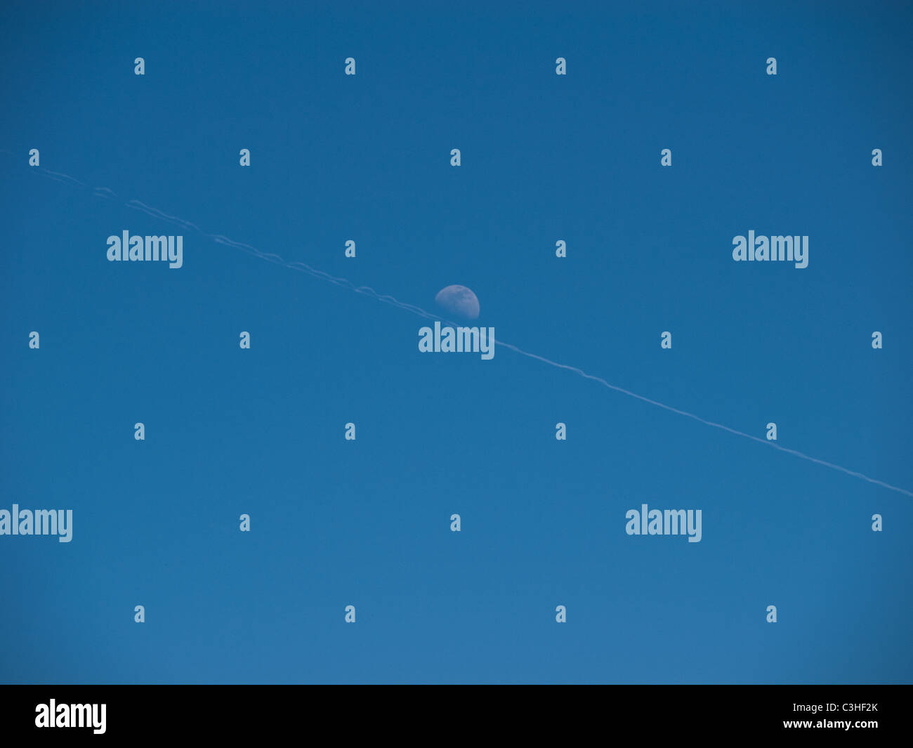 moon rising above the trail of a jetliner as though rising over the ...