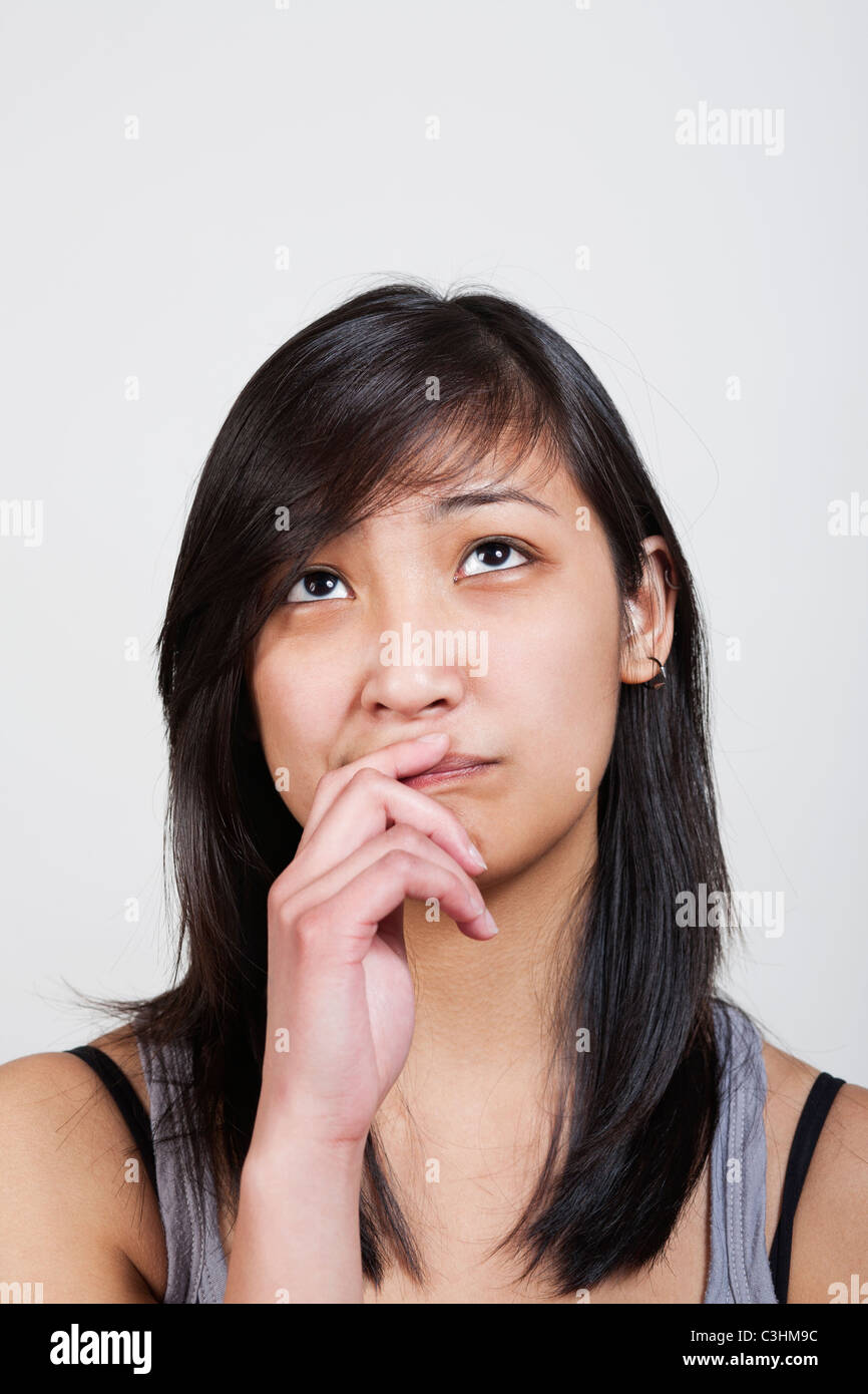 Young woman daydreaming with finger on face over colored background ...
